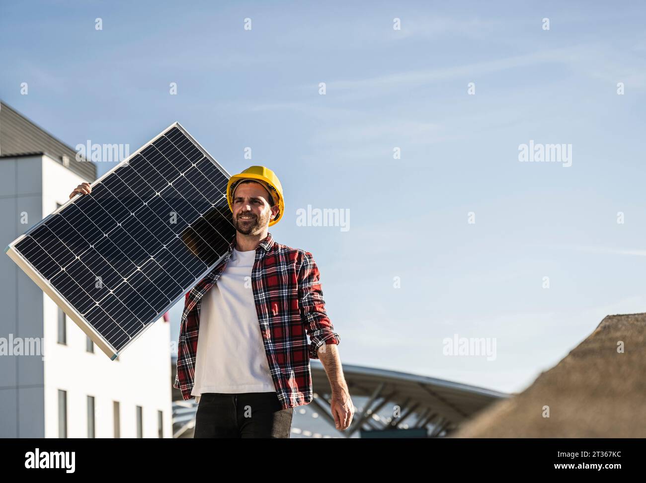Engineer wearing hardhat carrying solar panel on shoulder at terrace ...