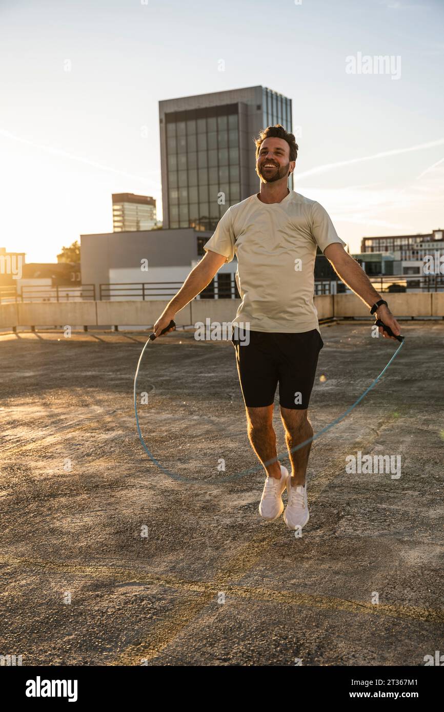 Smiling man jumping over rope at terrace Stock Photo - Alamy