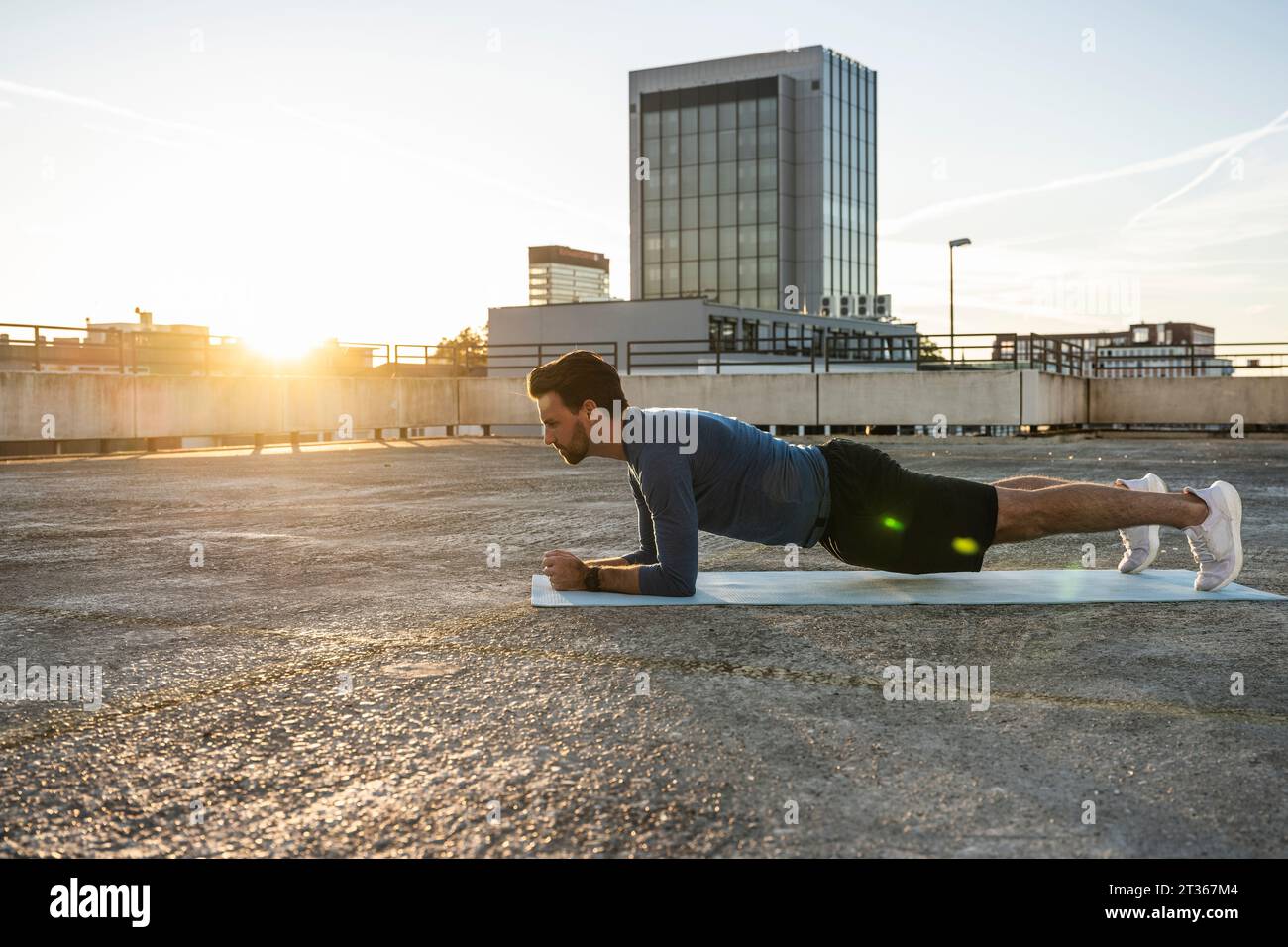 Active man practicing plank position on terrace at sunset Stock Photo ...