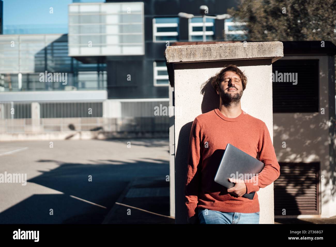 Businessman holding laptop leaning on column with eyes closed Stock ...