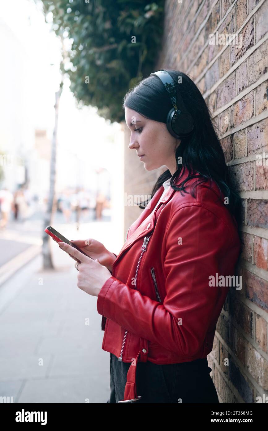 Woman wearing wireless headphones using smart phone near wall Stock ...