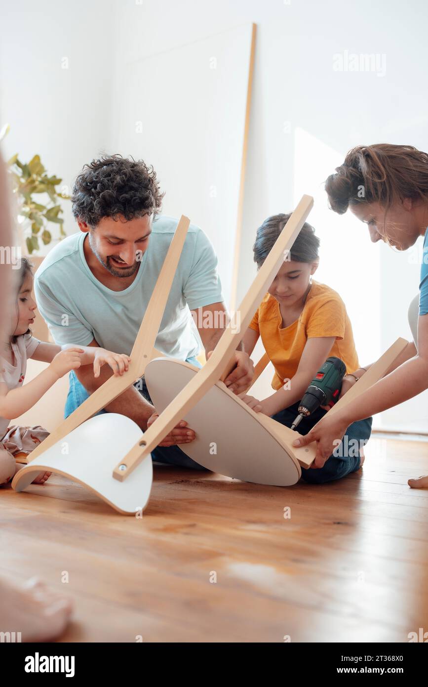 Happy family with woman using drill machine on wooden chair at home ...