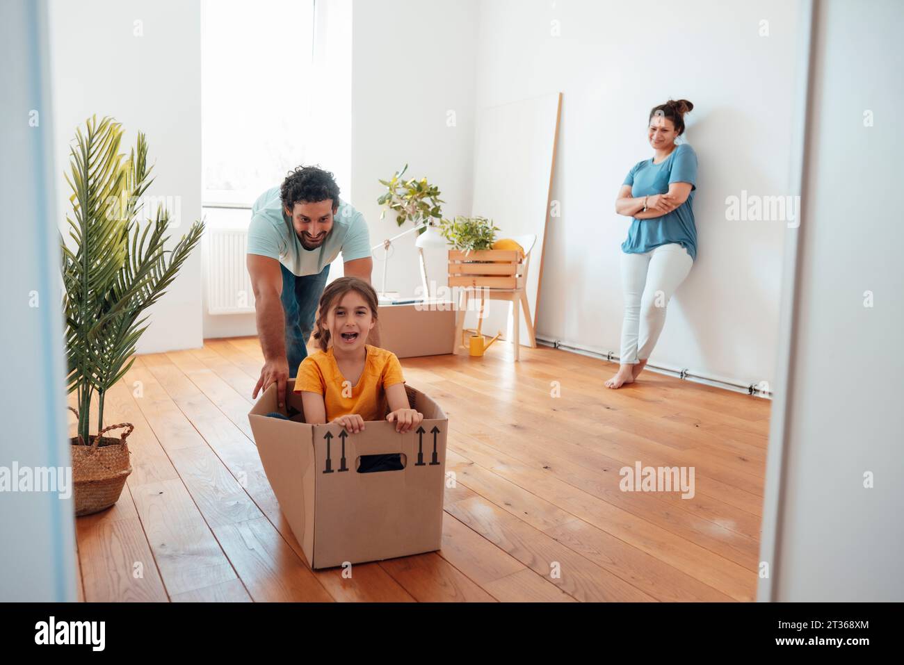 Smiling man pushing daughter sitting in cardboard box with woman ...
