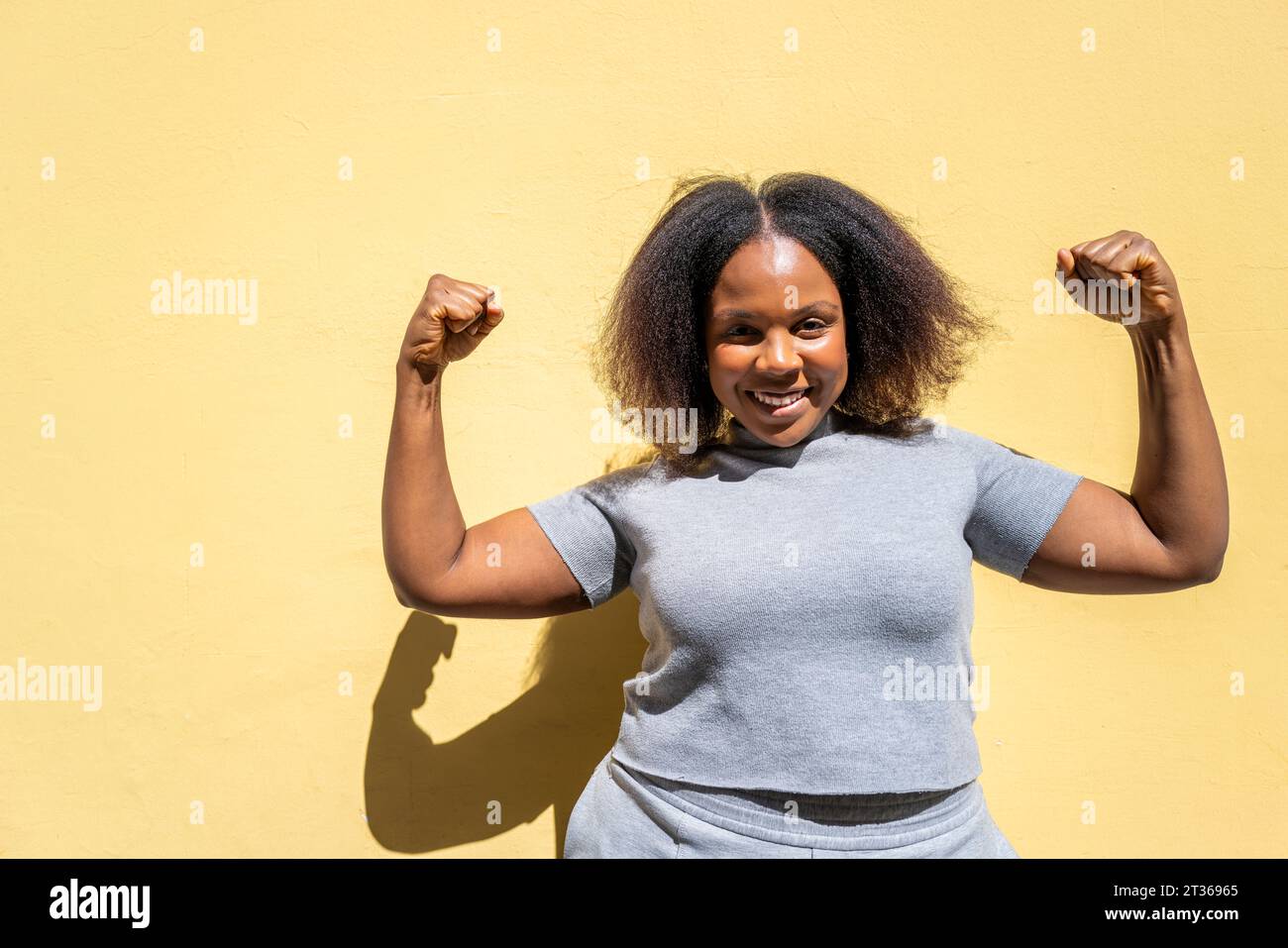 Smiling woman flexing muscles in front of wall Stock Photo - Alamy