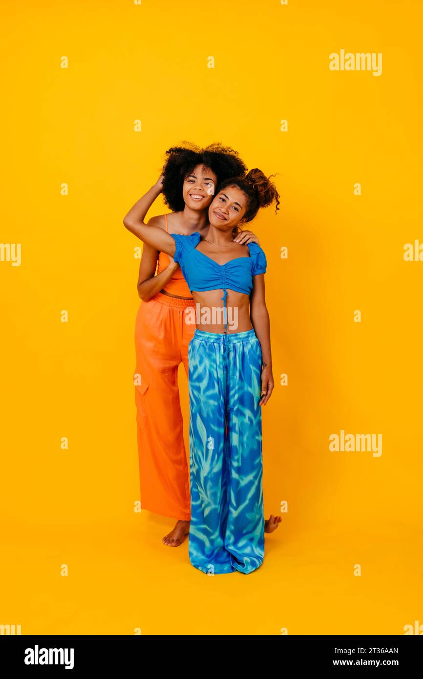 Smiling multiracial friends standing together against yellow background ...