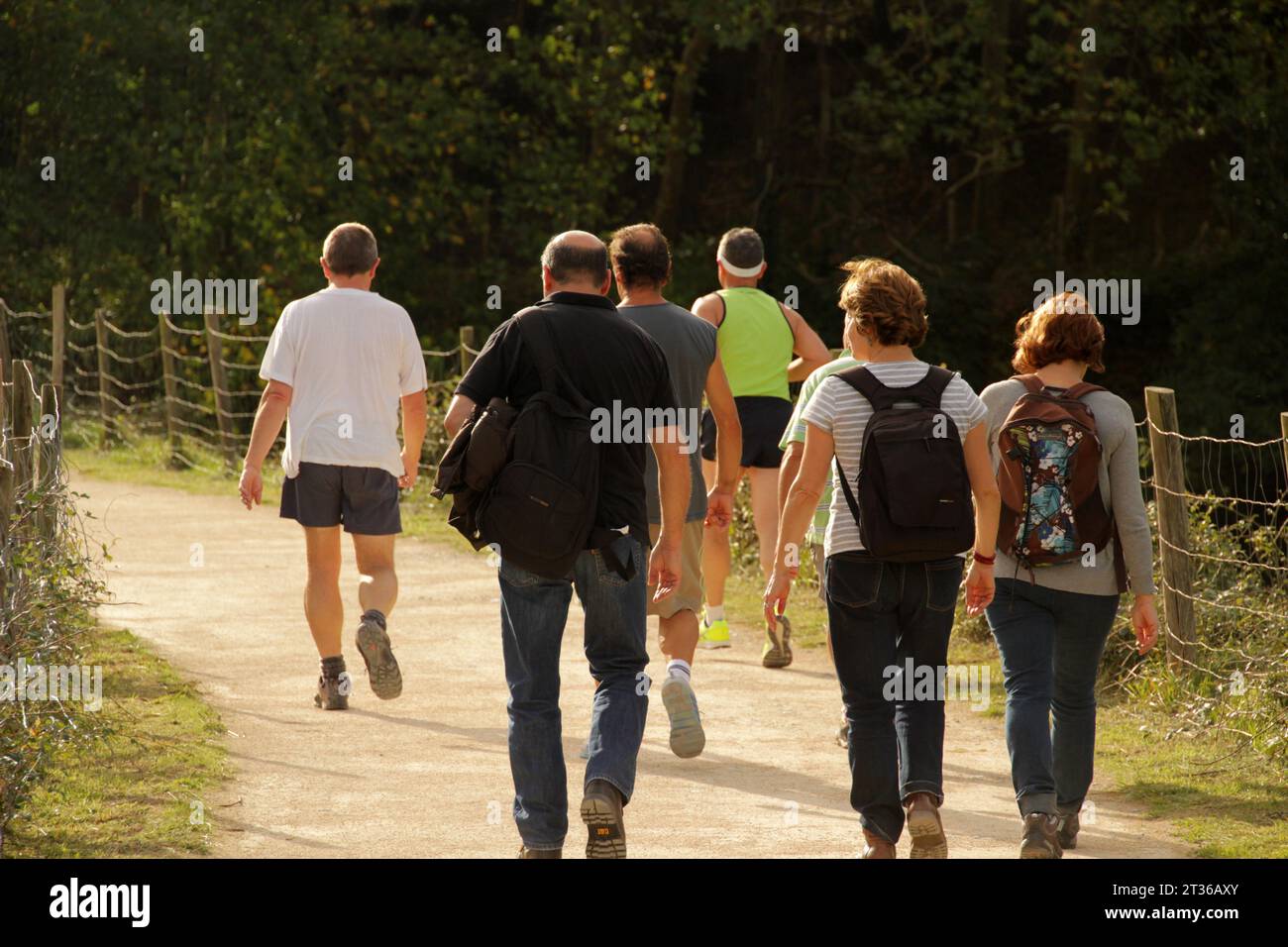 A diverse group of people walking down a dusty path between two wooden ...