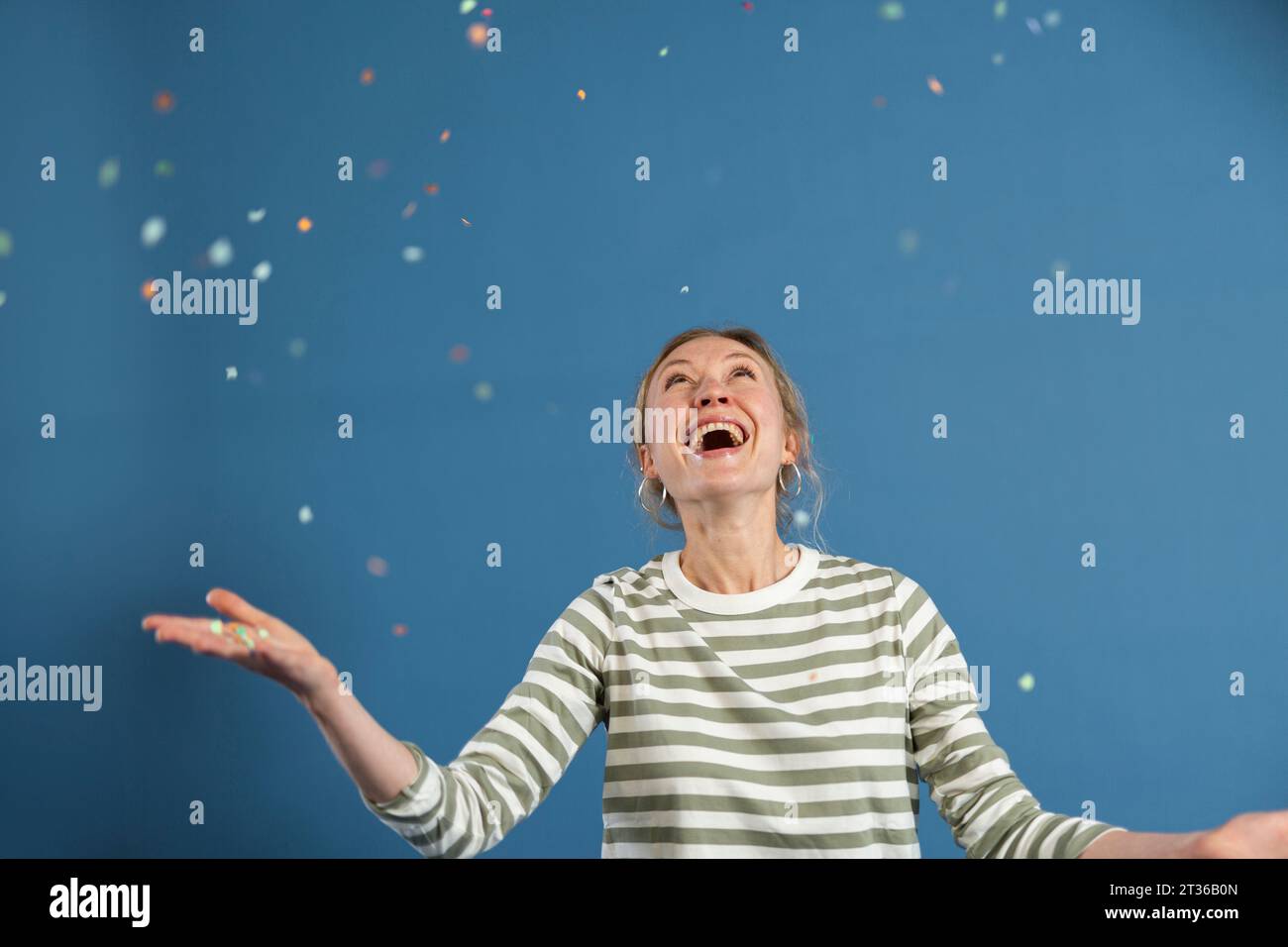 Happy woman throwing confetti against blue background Stock Photo - Alamy