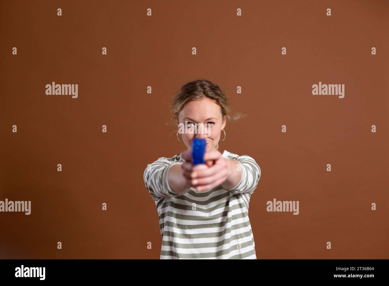 Blond woman holding toy gun over brown background Stock Photo - Alamy