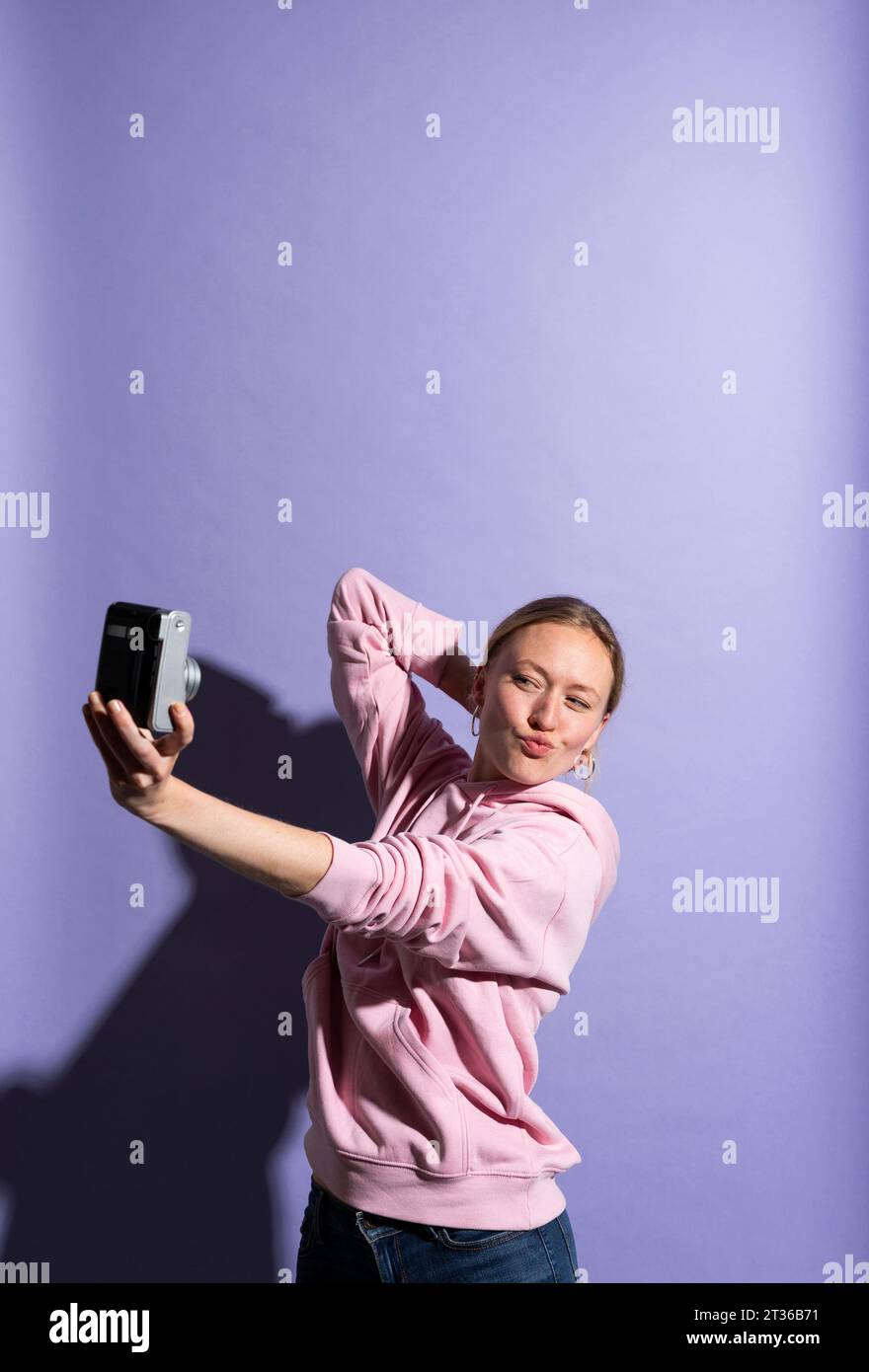 Woman puckering and photographing herself through camera against purple ...
