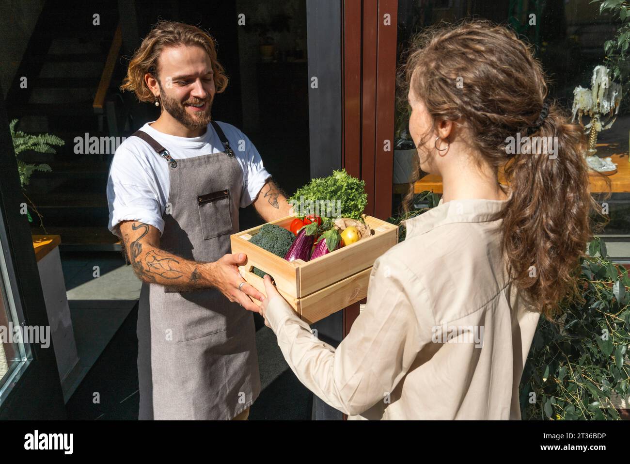 Young owner giving vegetable crate to customer Stock Photo - Alamy