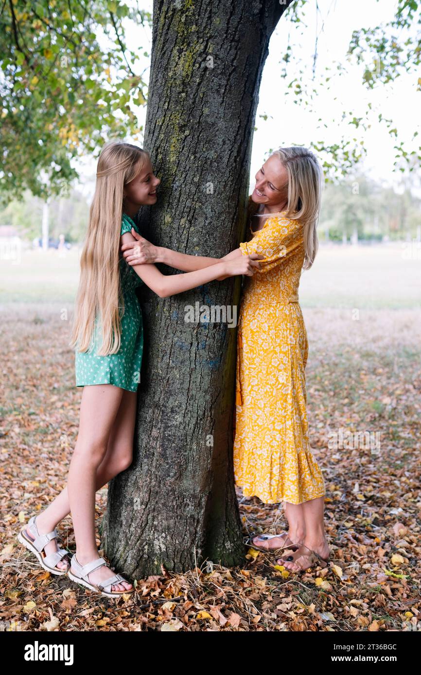 Mother and daughter playing around tree trunk in park Stock Photo - Alamy