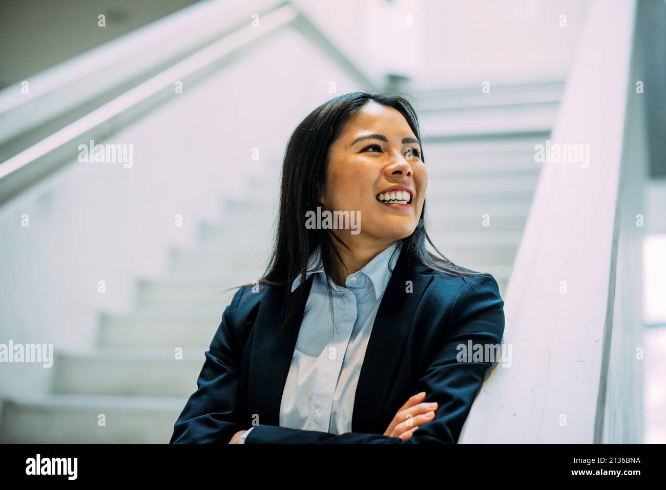 Happy beautiful businesswoman with arms crossed leaning on railing at ...
