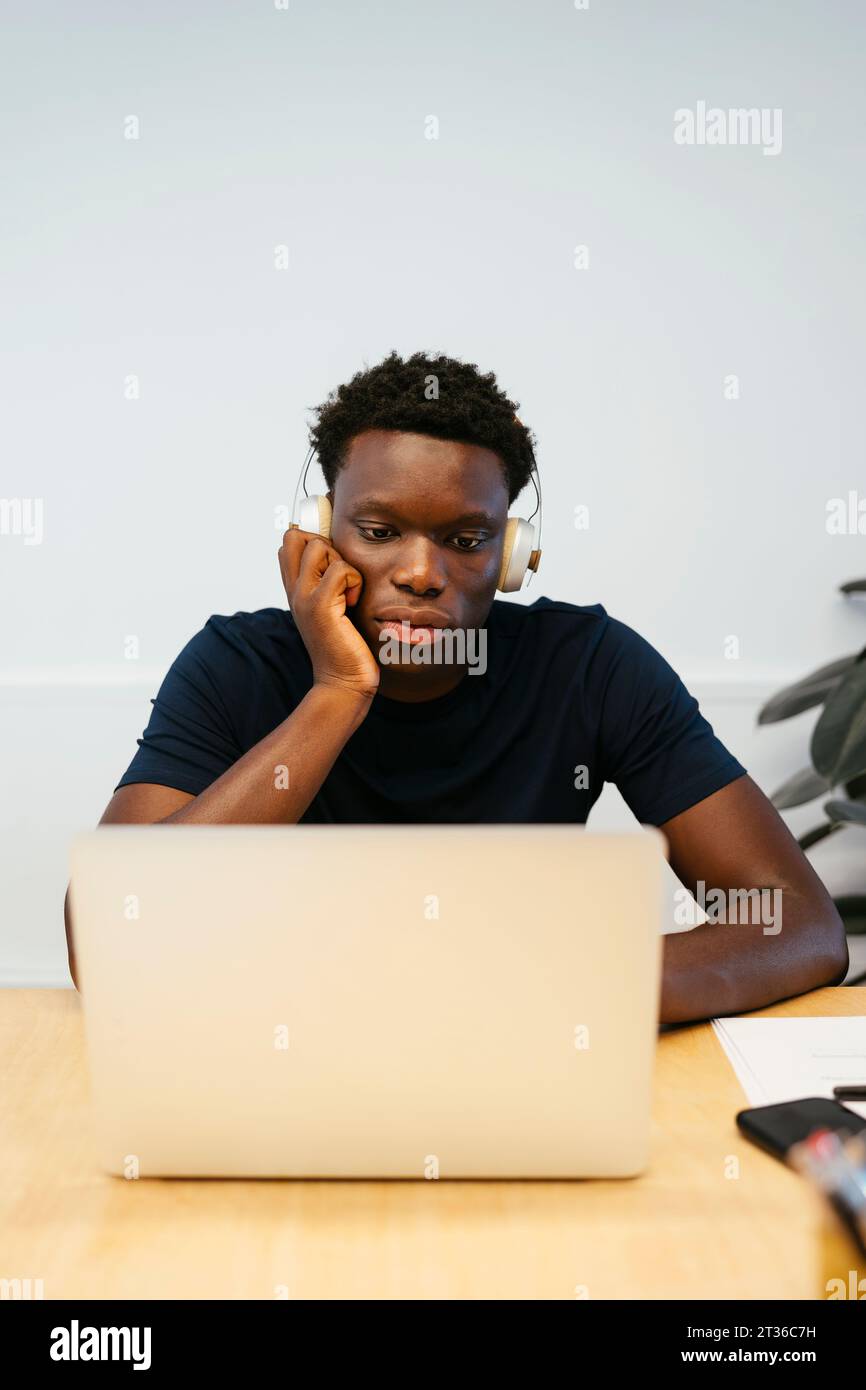 Student wearing wireless headphones and using laptop at desk Stock ...