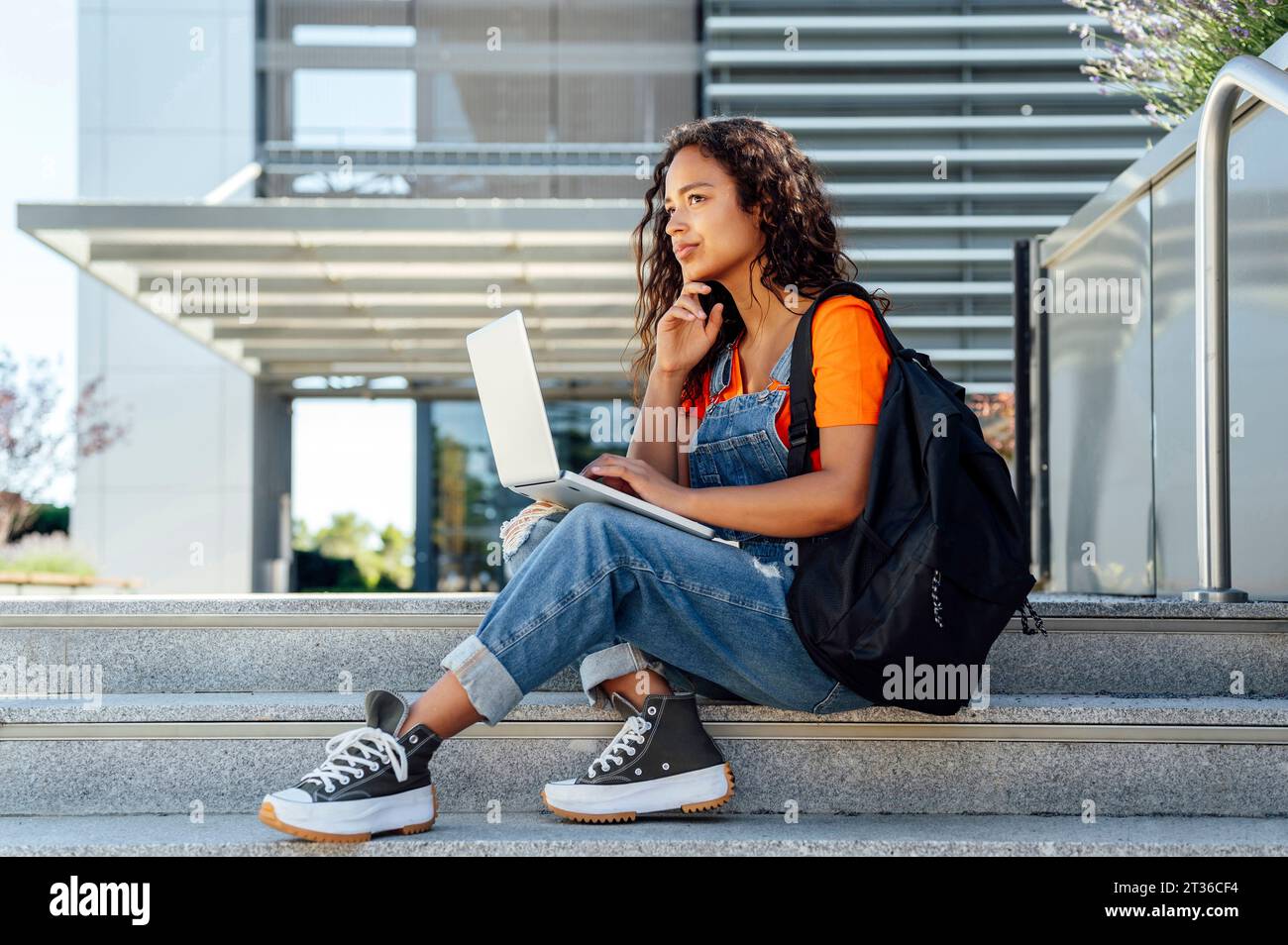 Contemplative student sitting with laptop on steps at campus Stock ...