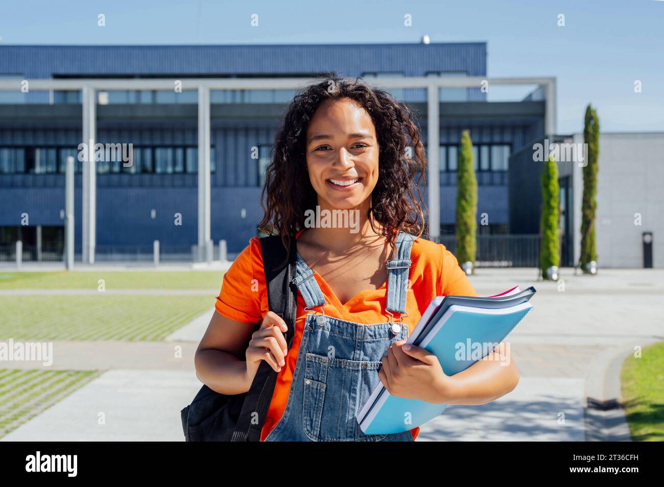 Smiling student with backpack holding books in front of building Stock ...