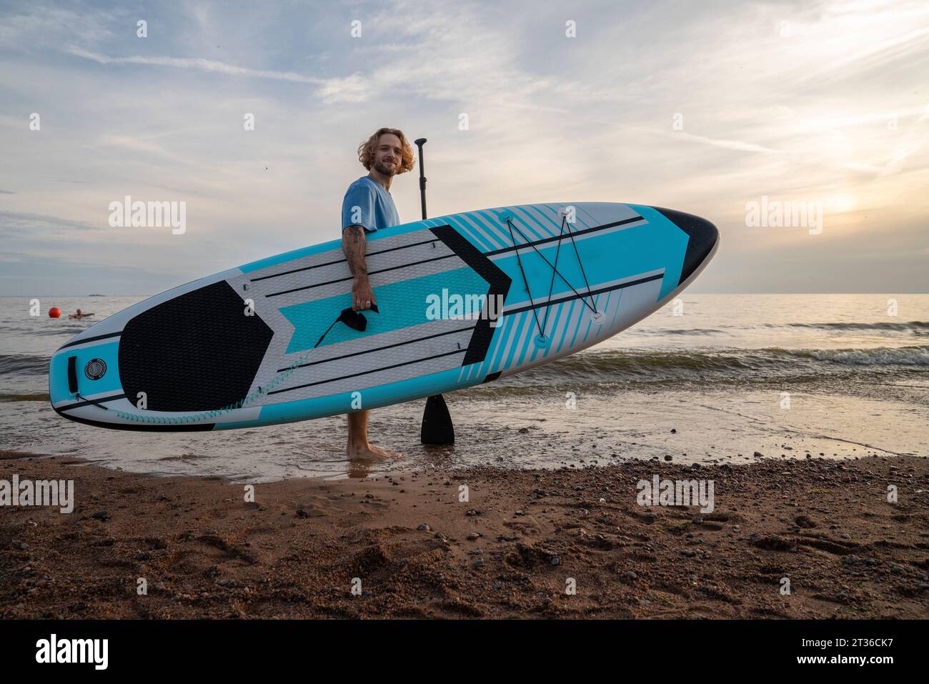 Young man carrying paddleboard at beach Stock Photo - Alamy