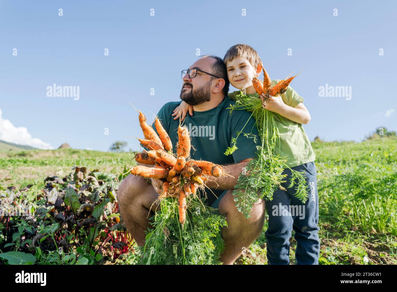 Boy with arm around father holding carrots in vegetable garden Stock ...