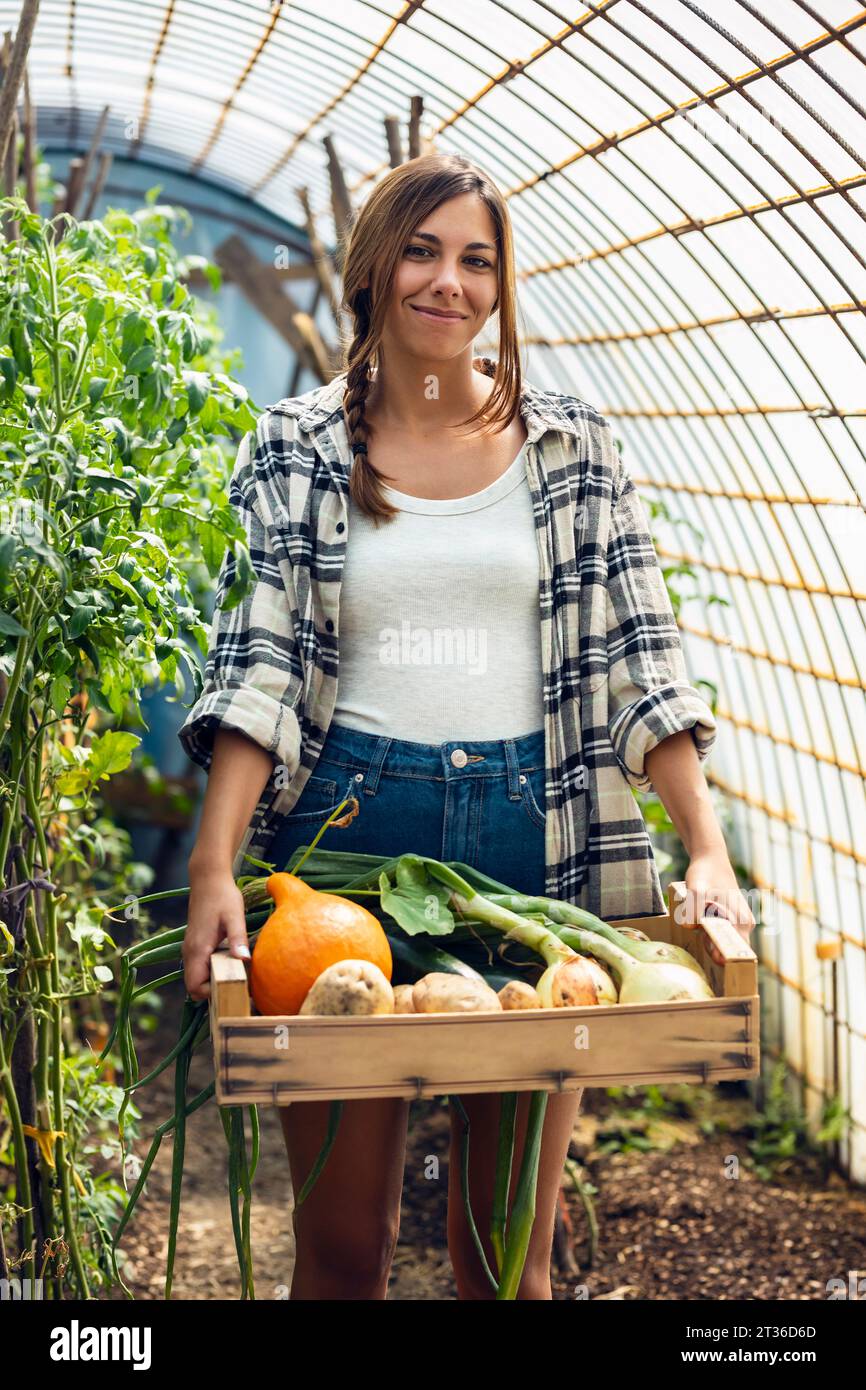 Smiling young farm worker with freshly harvested vegetables in crate at ...