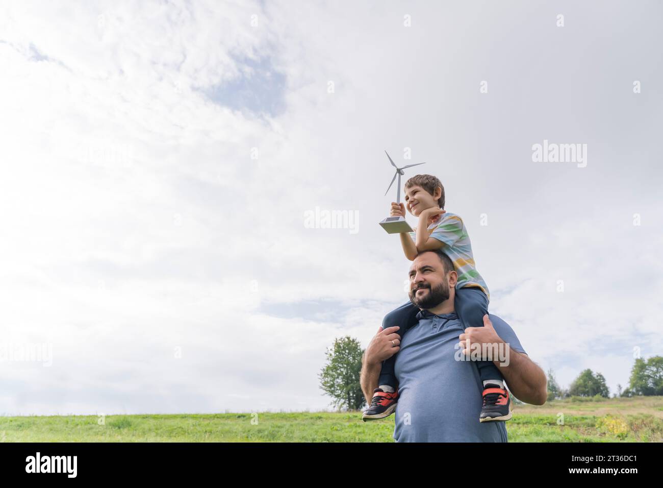 Man carrying son on shoulders with wind turbine model in front of ...