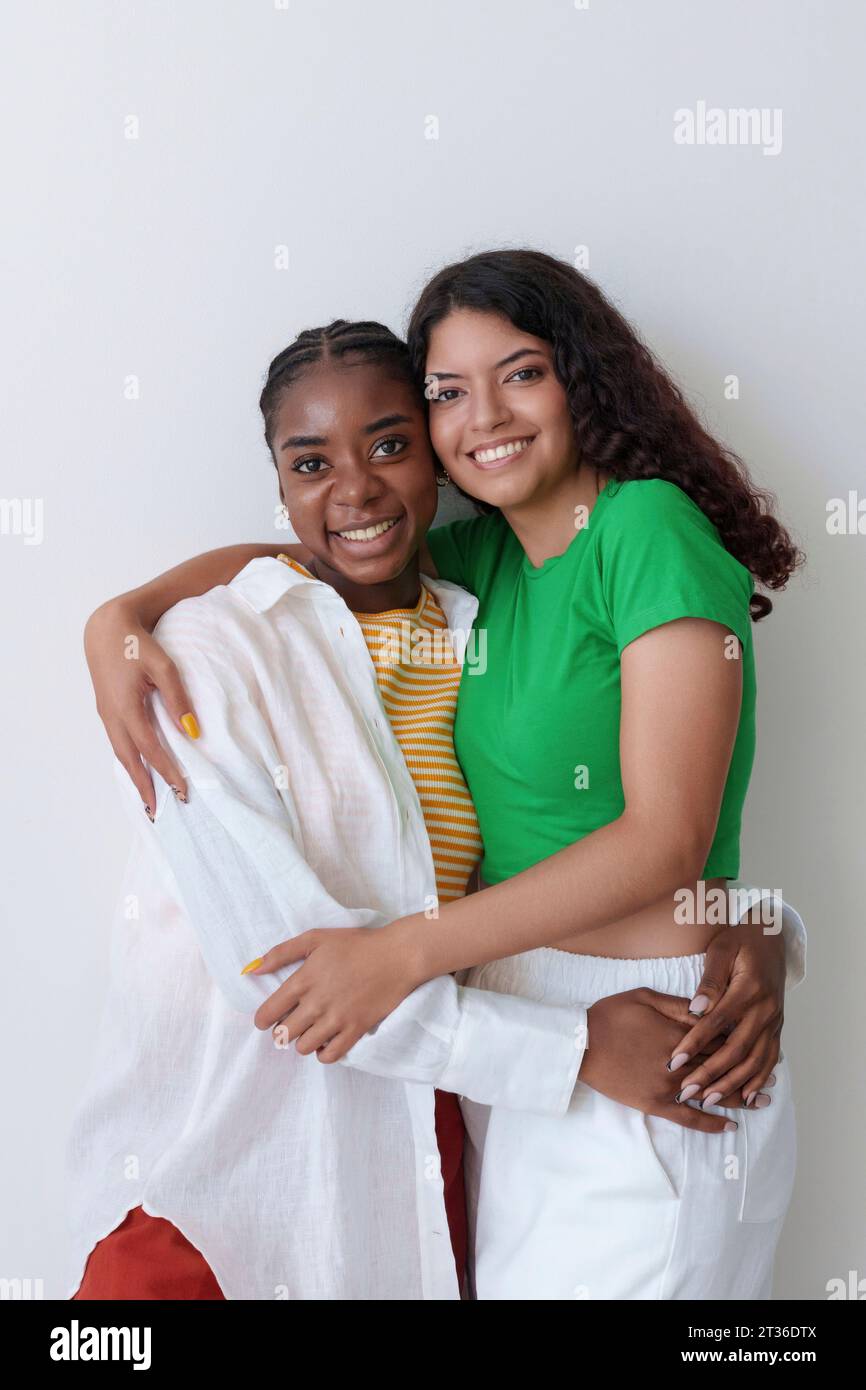 Smiling friends hugging in front of wall Stock Photo - Alamy