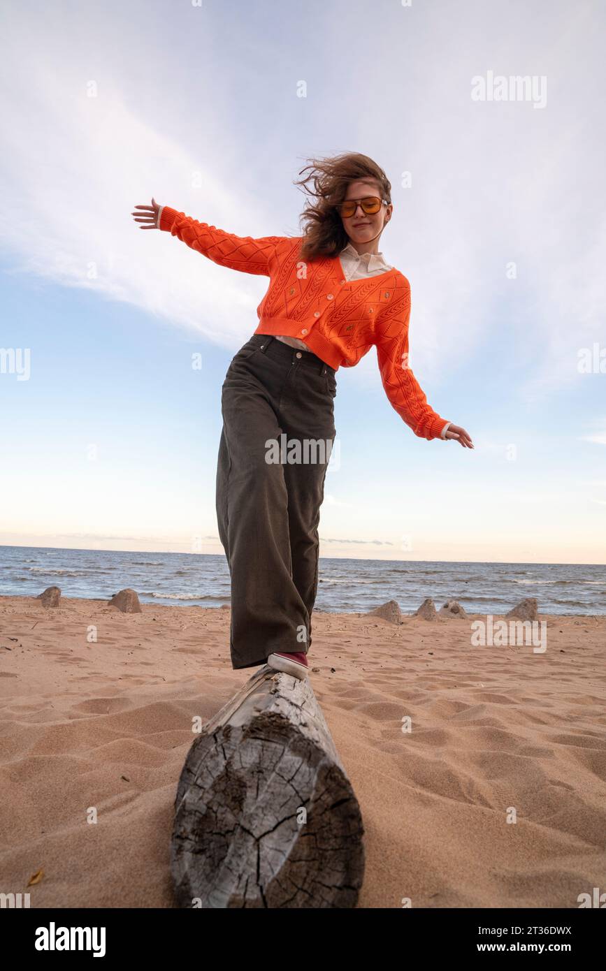 Woman with arms outstretched walking on wooden log at beach Stock Photo ...