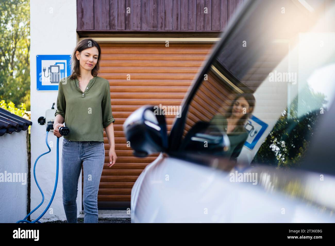 Woman holding power cord standing next to electric car at station Stock ...
