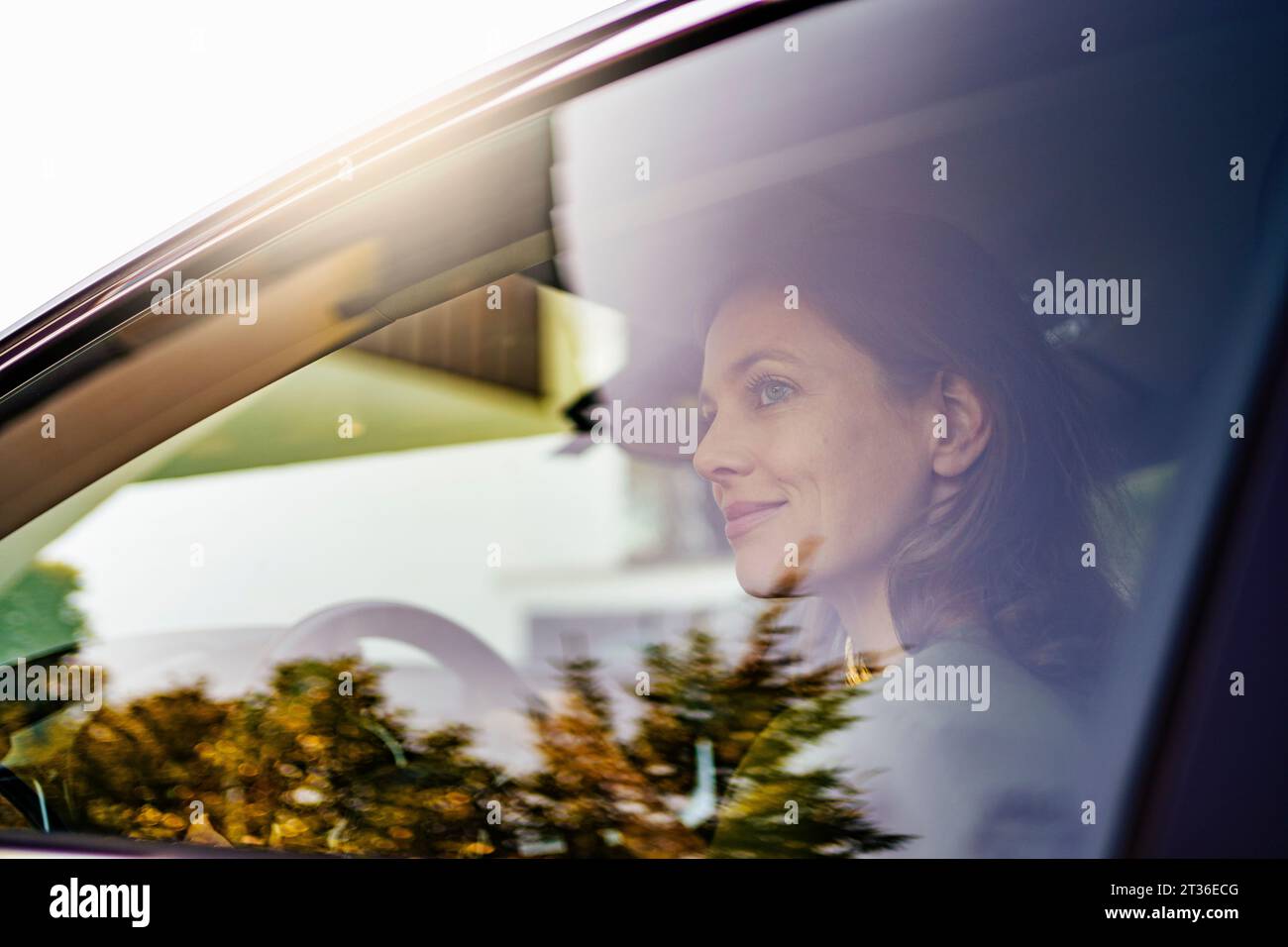 Smiling woman driving electric car seen through window Stock Photo - Alamy
