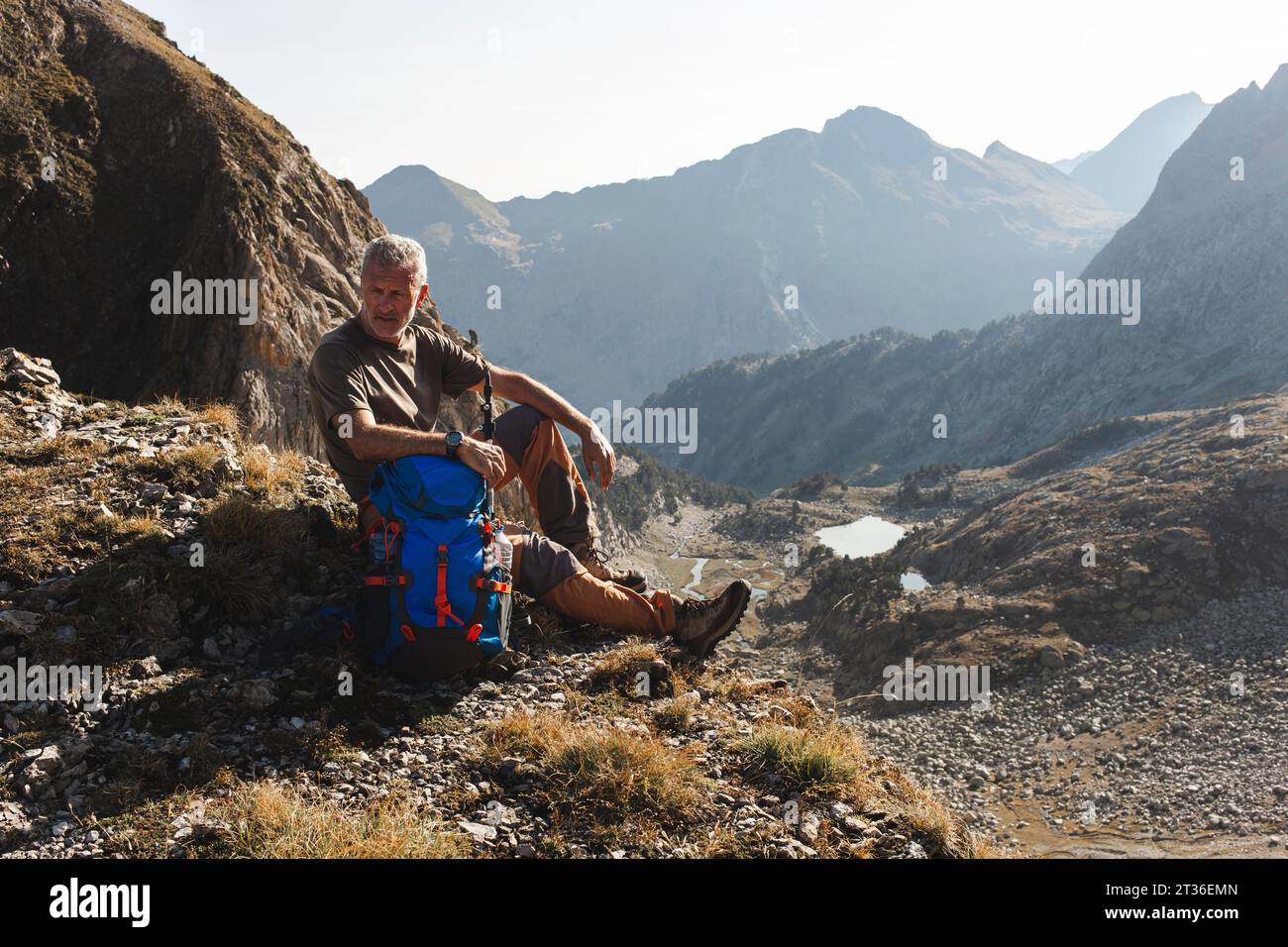 Mature man sitting with backpack in front of mountains Stock Photo - Alamy