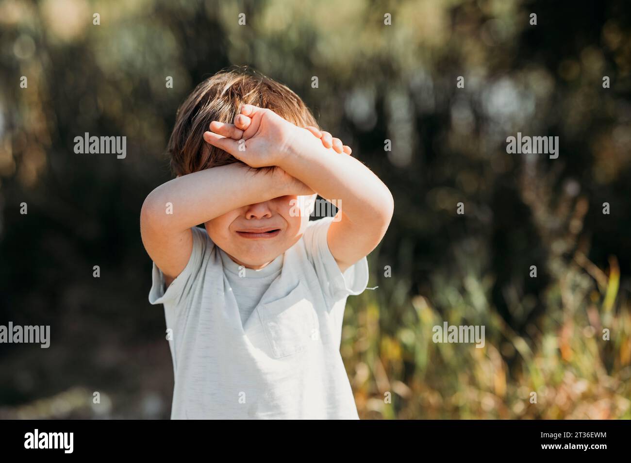 Boy crying with hands on eyes in field Stock Photo - Alamy