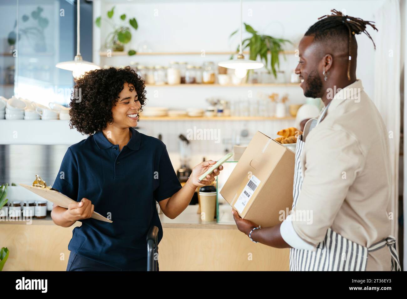 Smiling delivery woman scanning QR code from package in cafe Stock ...