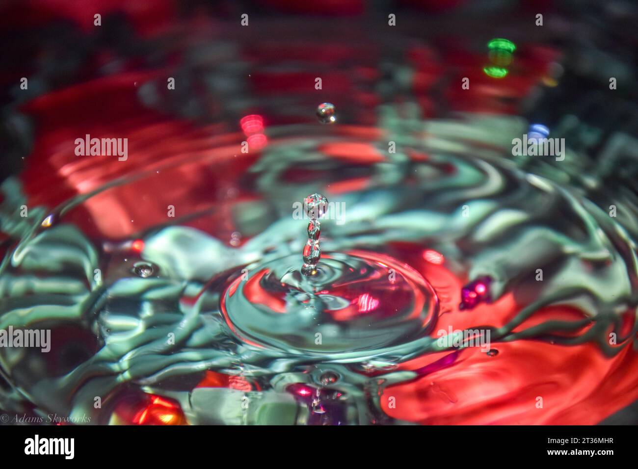 A close-up of a single drop of water hitting a red-coloured plastic ...