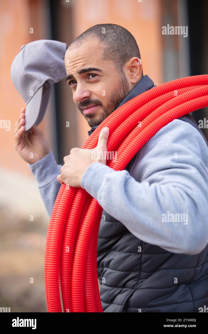 tradesman holding a reel of red pipe on his shoulder Stock Photo - Alamy