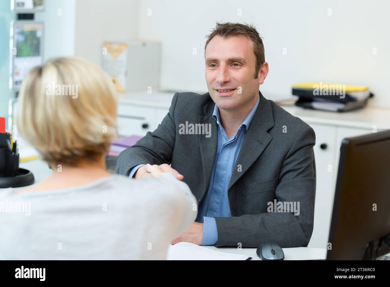 estate agent shaking hands with client at office desk Stock Photo - Alamy