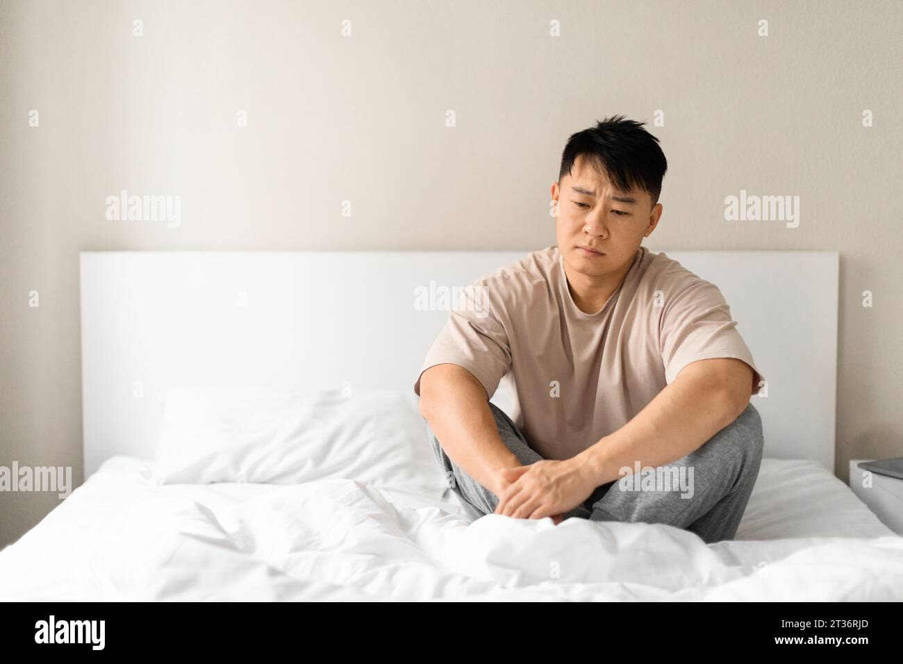 Frustrated mature chinese man in pajamas sitting on bed Stock Photo - Alamy