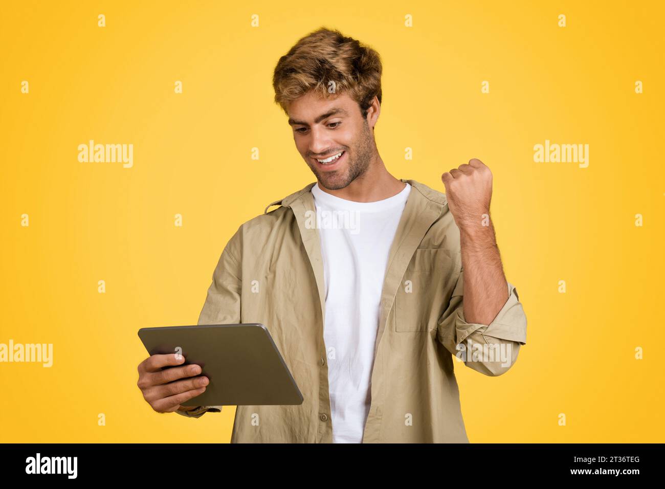 Young European man gestures yes with tablet on yellow studio backdrop ...