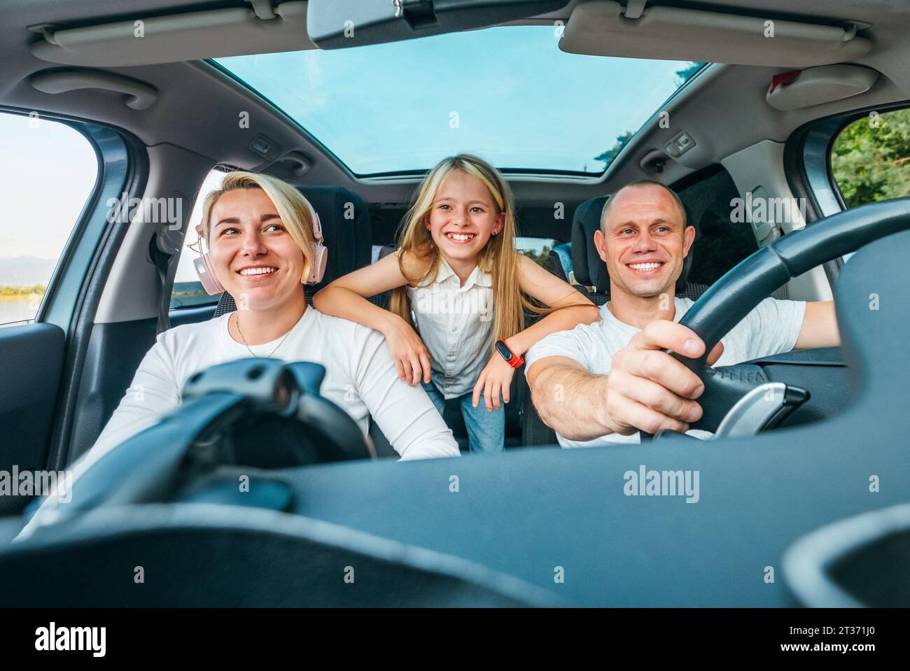 Happy young couple with daughter inside the modern car with panoramic roof during auto trop ...