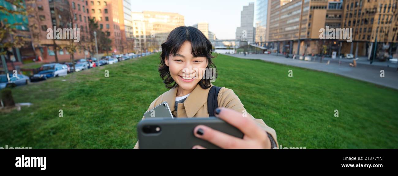 Happy young woman, student takes selfie on street, holds her tablet and ...