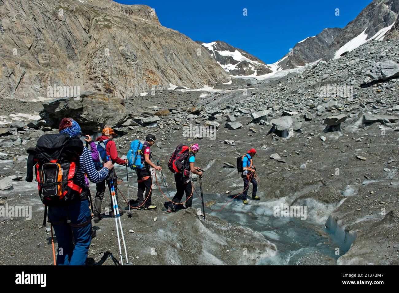 Group of hikers on a glacier hike crossing the rock scree at the edge ...