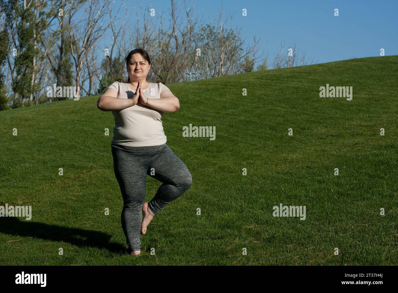 overweight middle-aged woman practices yoga outdoors barefoot, doing ...