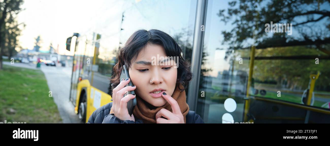 Perplexed asian girl, talks on mobile phone with concerned, thoughtful ...