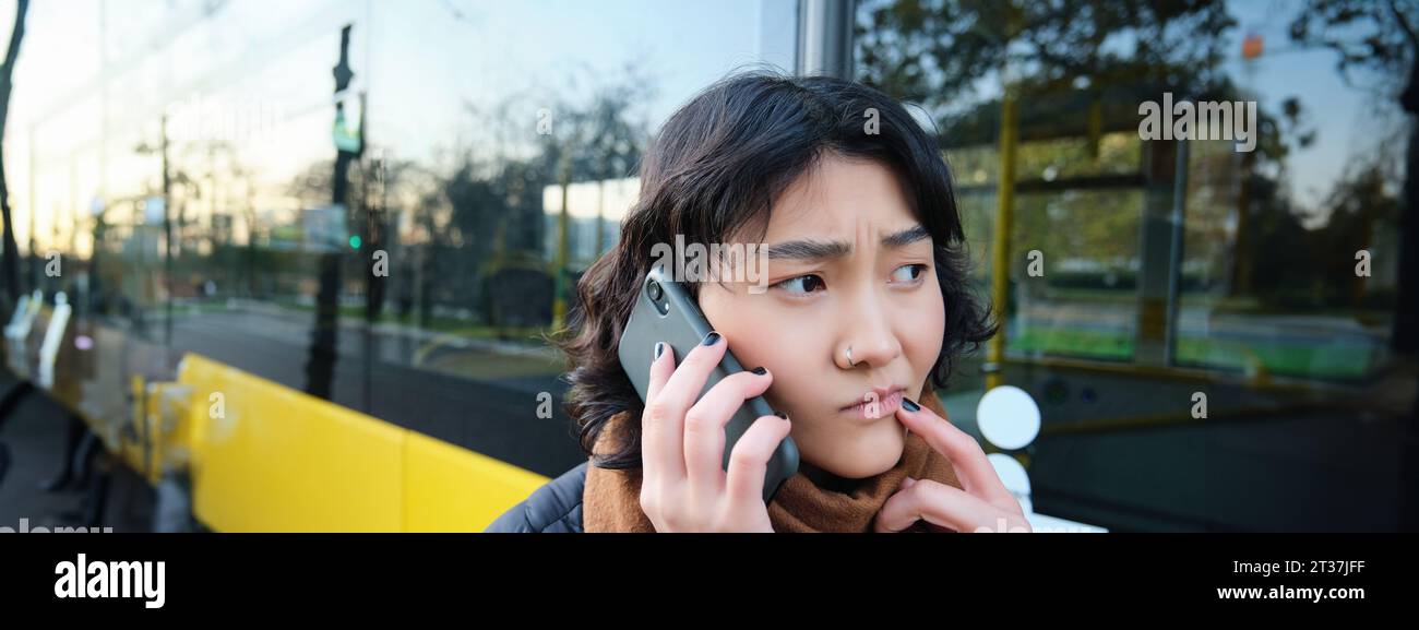 Perplexed asian girl, talks on mobile phone with concerned, thoughtful ...