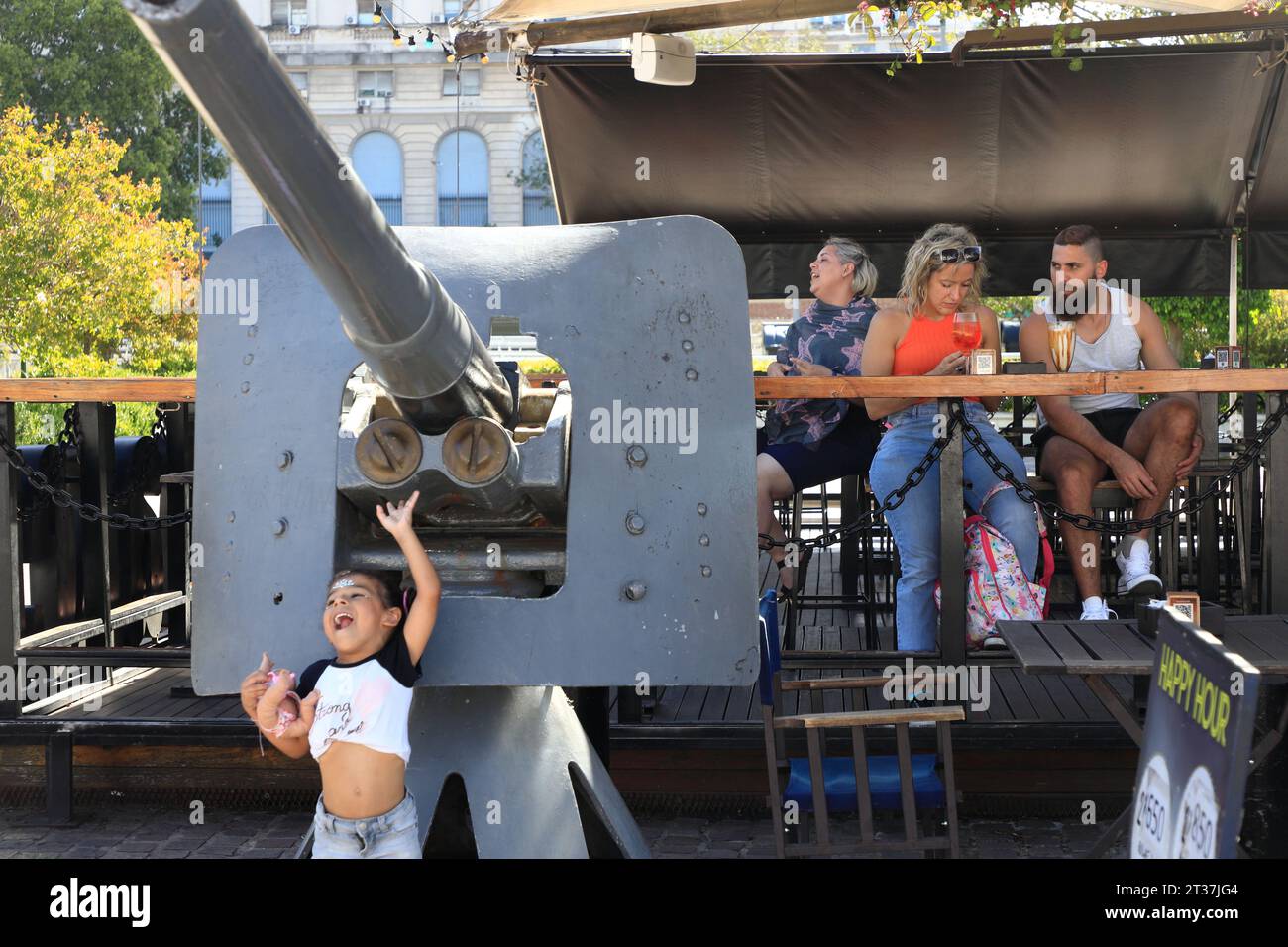 Customers relaxing in a outdoor cafe with a child jumping in front of ...
