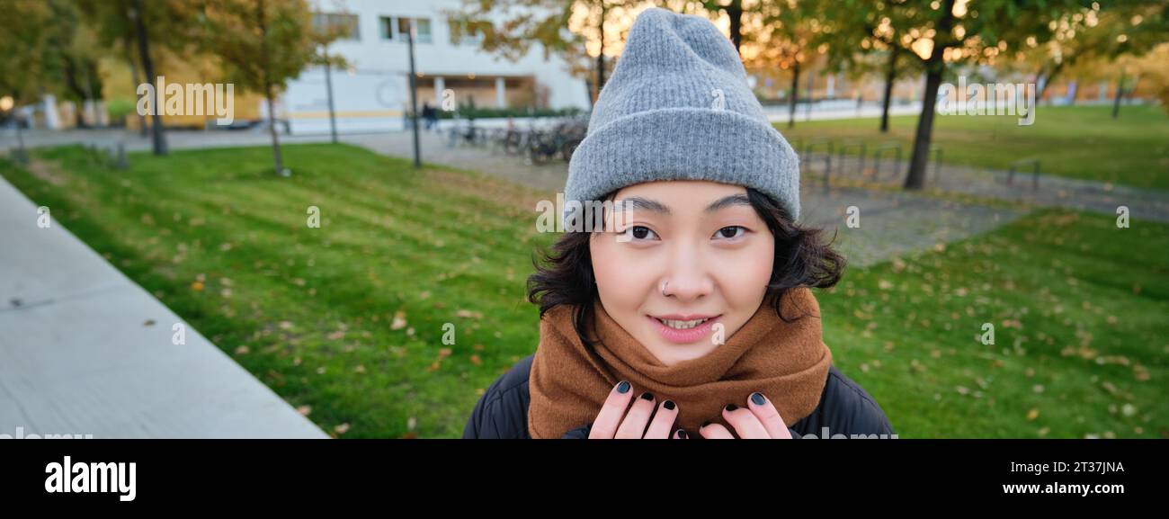 Portrait of cute asian girl in hat and scarf, walks around town in ...