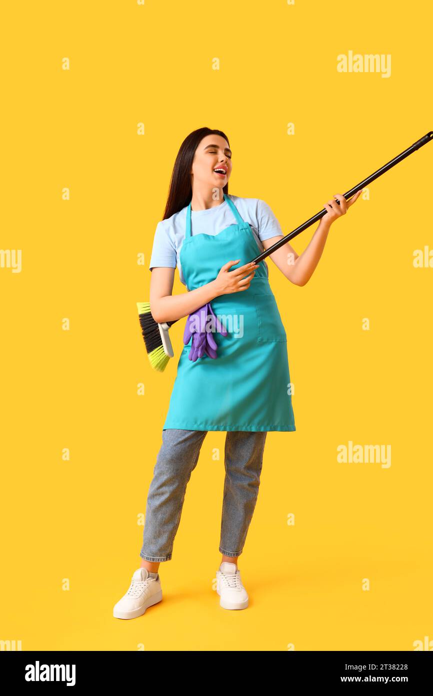 Female janitor with broom singing on yellow background Stock Photo - Alamy