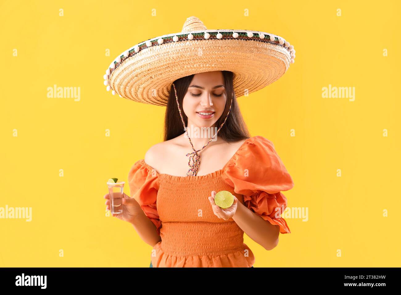 Beautiful young Mexican woman in sombrero and with tequila on yellow ...