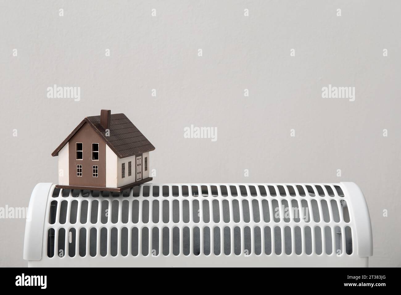 Figure of house on electric convector heater near white wall at home ...