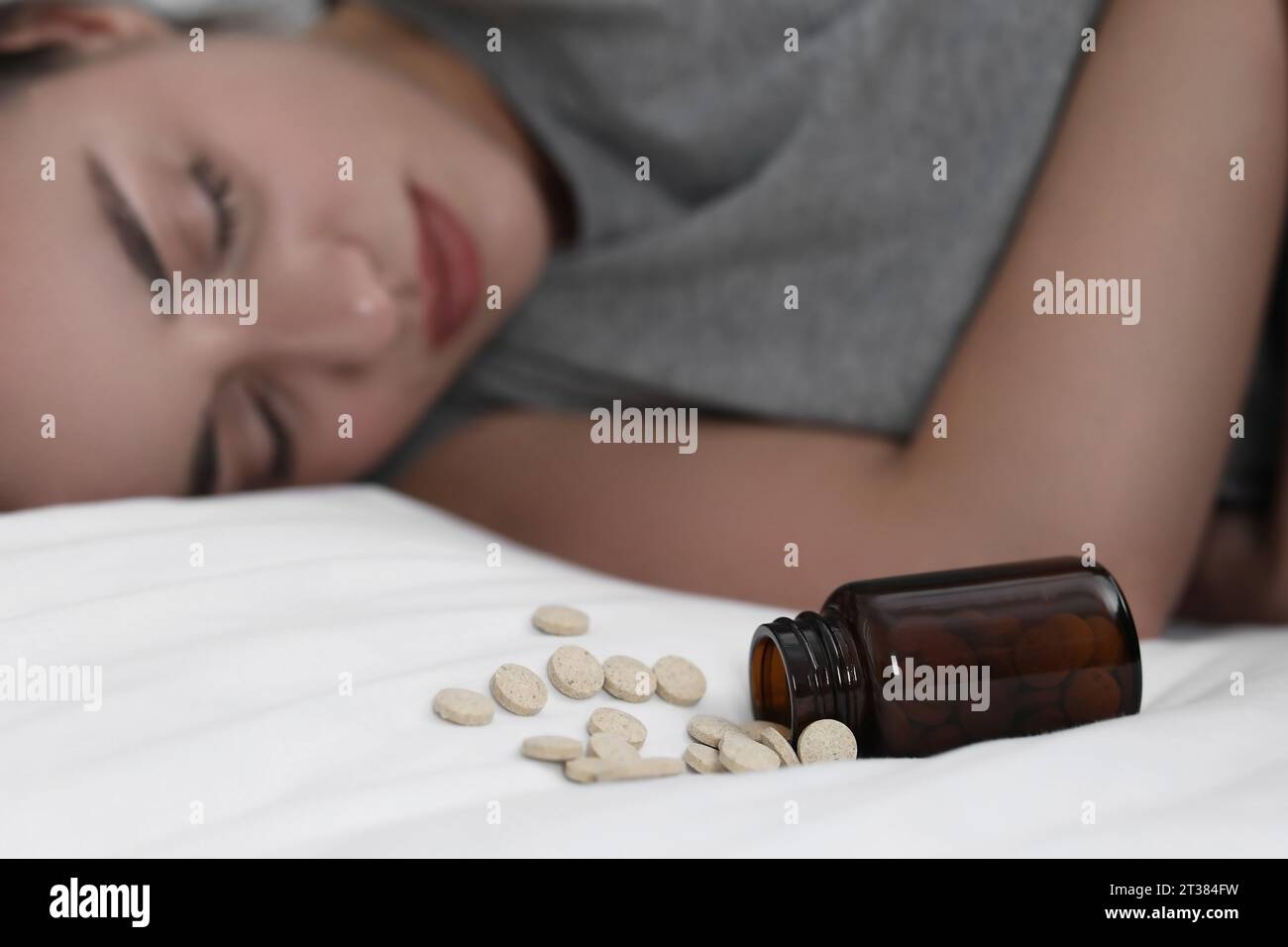 Depressed woman sleeping on bed near overturned bottle with antidepressants, selective focus ...