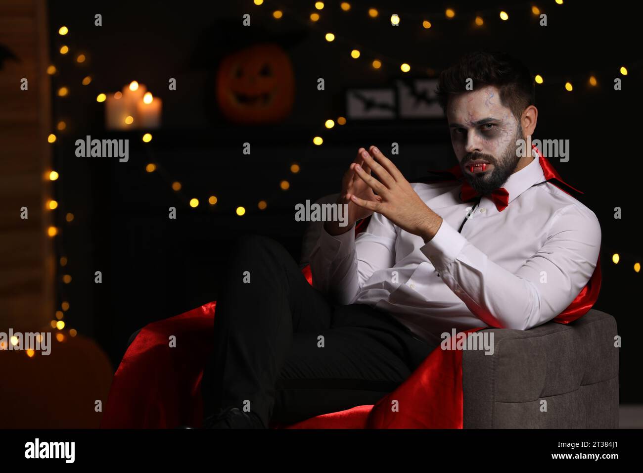Man in scary vampire costume against blurred lights indoors, space for ...