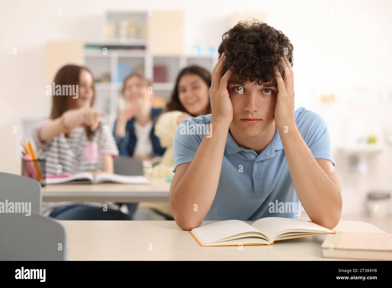 Teen problems. Lonely boy sitting separately from other students in ...