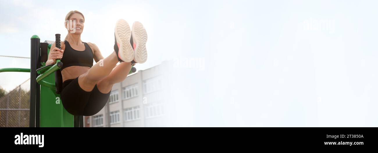 Happy woman doing abs exercise at outdoor gym, space for text. Banner ...